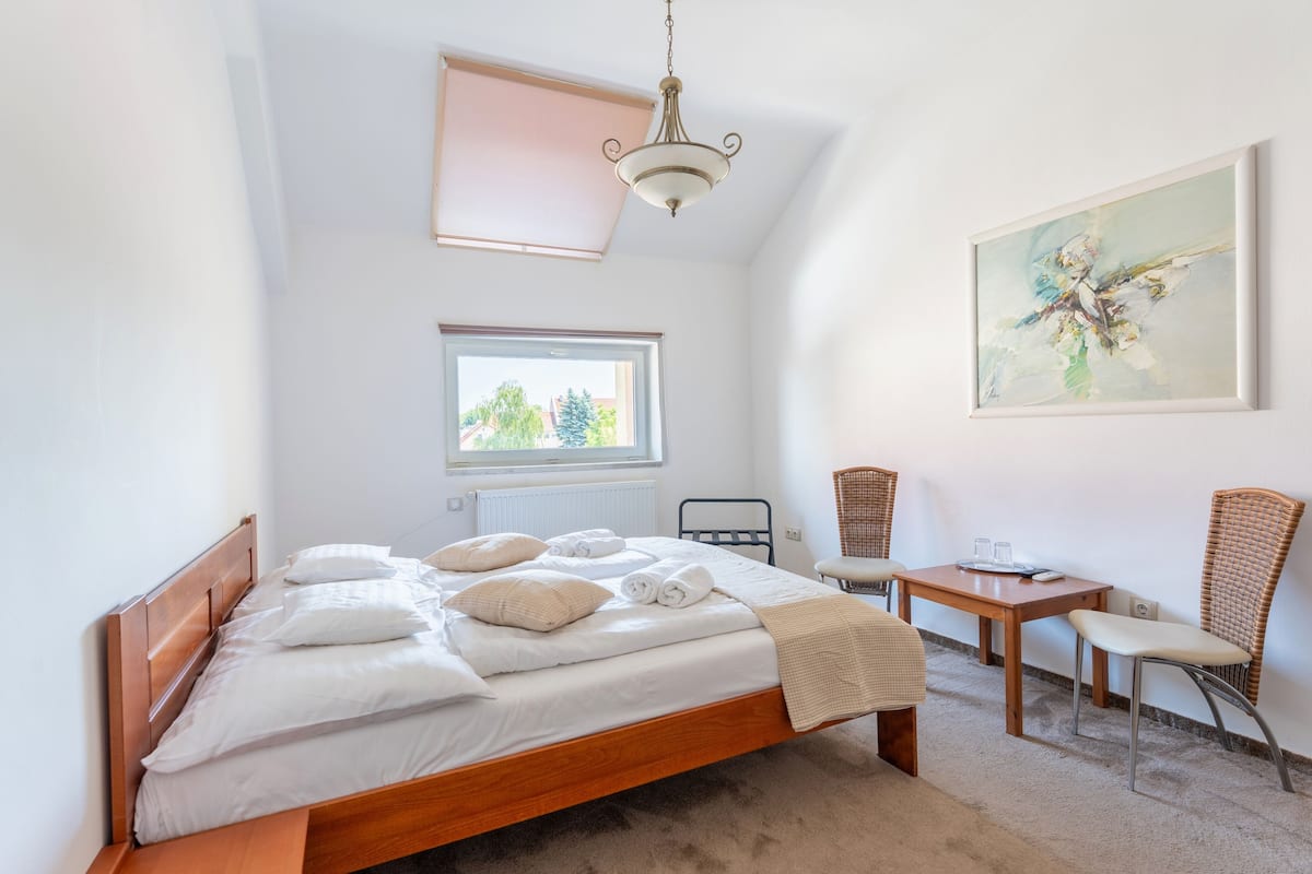 Um quarto com uma cama de madeira, uma janela, uma mesa com cadeiras e um quadro na parede.