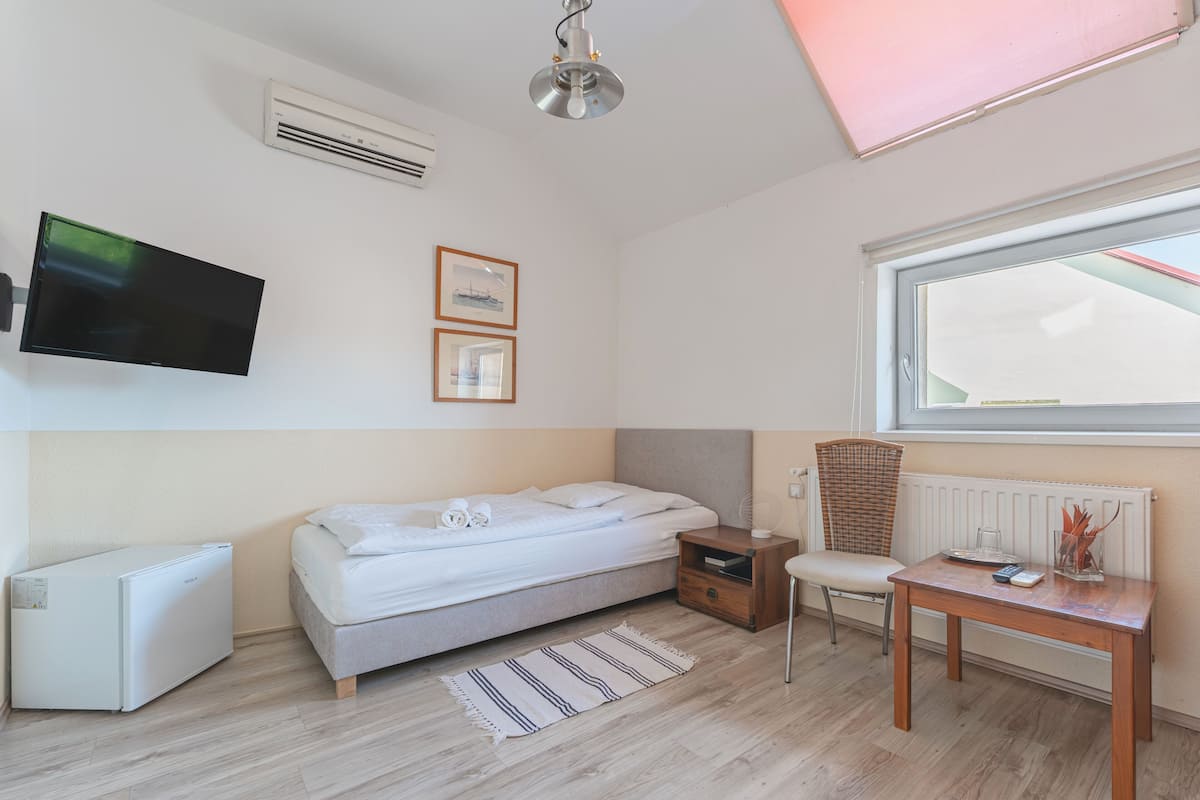 Quarto com cama, escrivaninha, cadeira, televisão e janela.