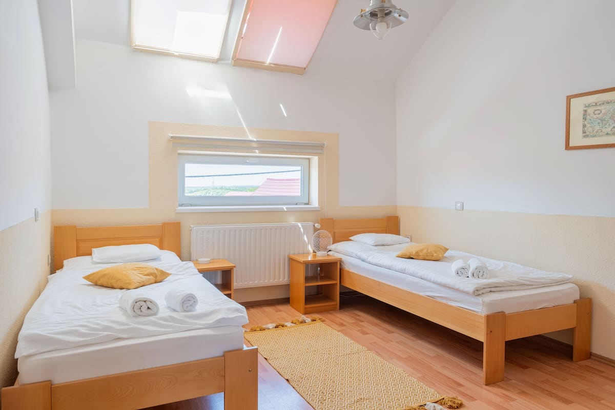 Quarto com duas camas de madeira, janela com vista, ventoinha no teto e radiador.