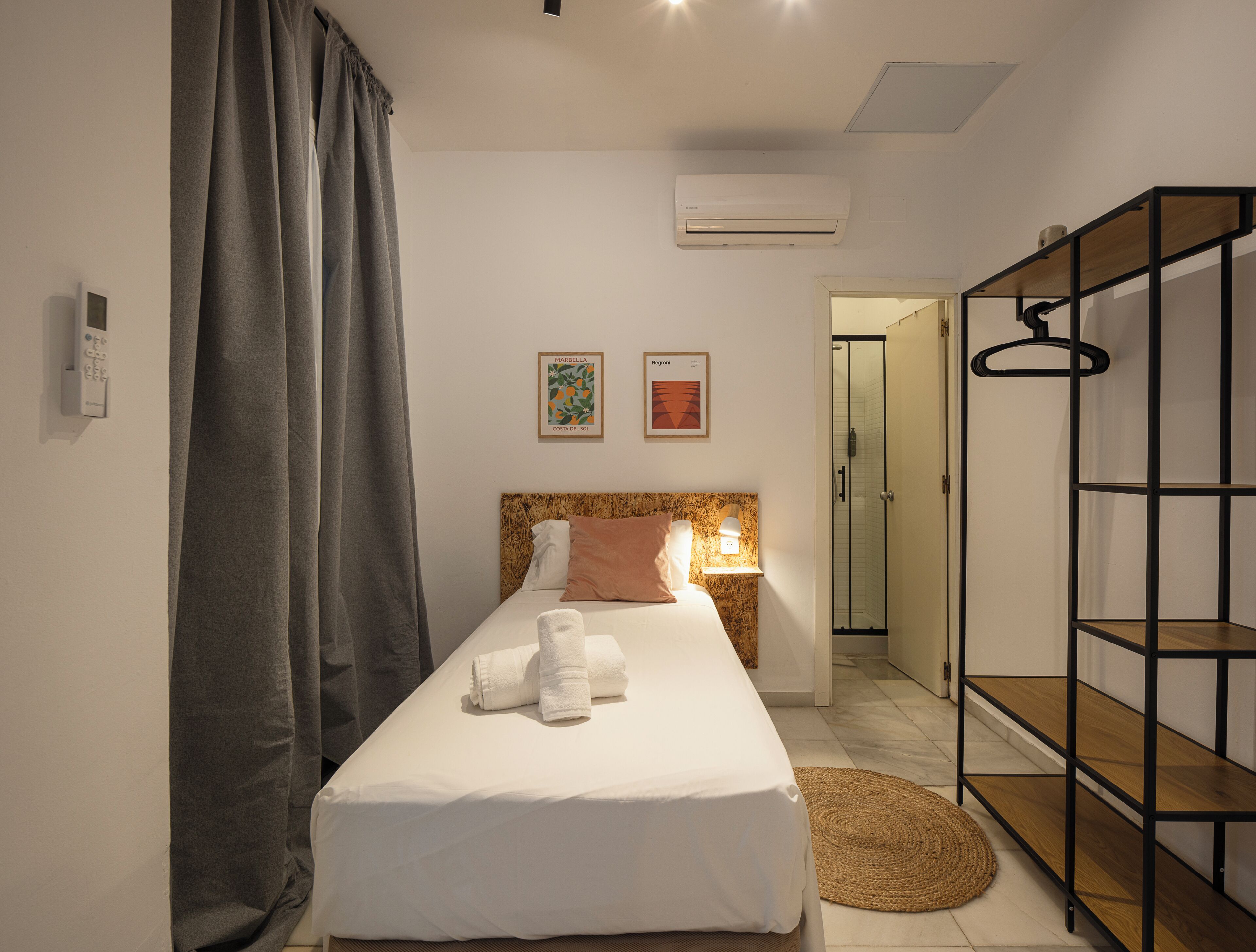 Quarto de hotel com cama, chuveiro, guarda-roupa e duas imagens penduradas na parede.