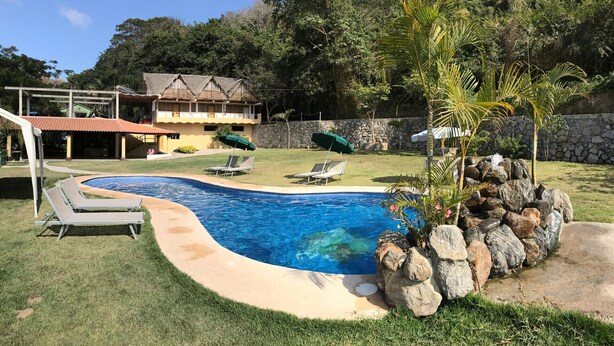 Piscina com espreguiçadeiras, cascata e parede de pedra.