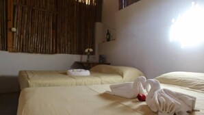 Quarto de hotel com duas camas, parede de bambu e uma pequena mesa com um vaso.