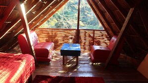 Um quarto de sótão aconchegante com teto de madeira, um sofá vermelho, uma pequena mesa com um vaso e um tapete vermelho.