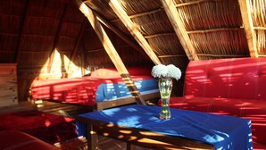 Um quarto com telhado de palha, móveis estofados vermelhos e uma mesa com toalha azul.