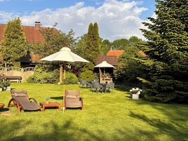 Um jardim bem cuidado com um gazebo, área de estar ao ar livre e churrasqueira.
