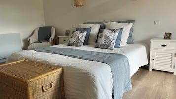 Quarto bem arrumado com cama, mesas de cabeceira, uma cadeira e um baú de vime.