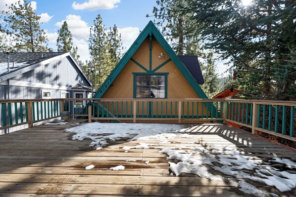 Uma cabana de madeira com telhado triangular, cercada por um deck de madeira e neve.