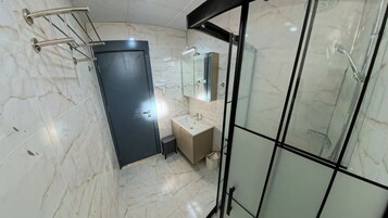 Um banheiro com piso de mármore, pia, espelho e chuveiro.