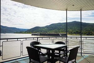 Mesa e cadeiras em um deck com vista para um rio e montanhas.