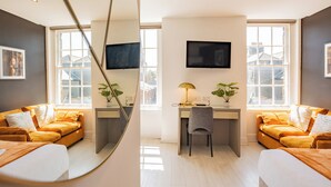 Quarto moderno com dois sofás amarelos, uma escrivaninha com cadeira, televisão e janelas amplas.