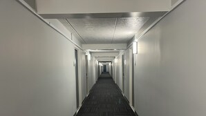 Corredor longo e estreito de hotel, com piso coberto por carpete e portas em ambos os lados, dando acesso aos quartos.