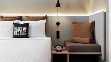 Quarto de hotel moderno com uma cama, uma mesa de cabeceira com telefone e uma luminária na parede.