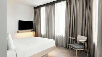 Quarto de hotel moderno com uma cama grande, televisão de tela plana na parede, uma mesinha e uma cadeira.