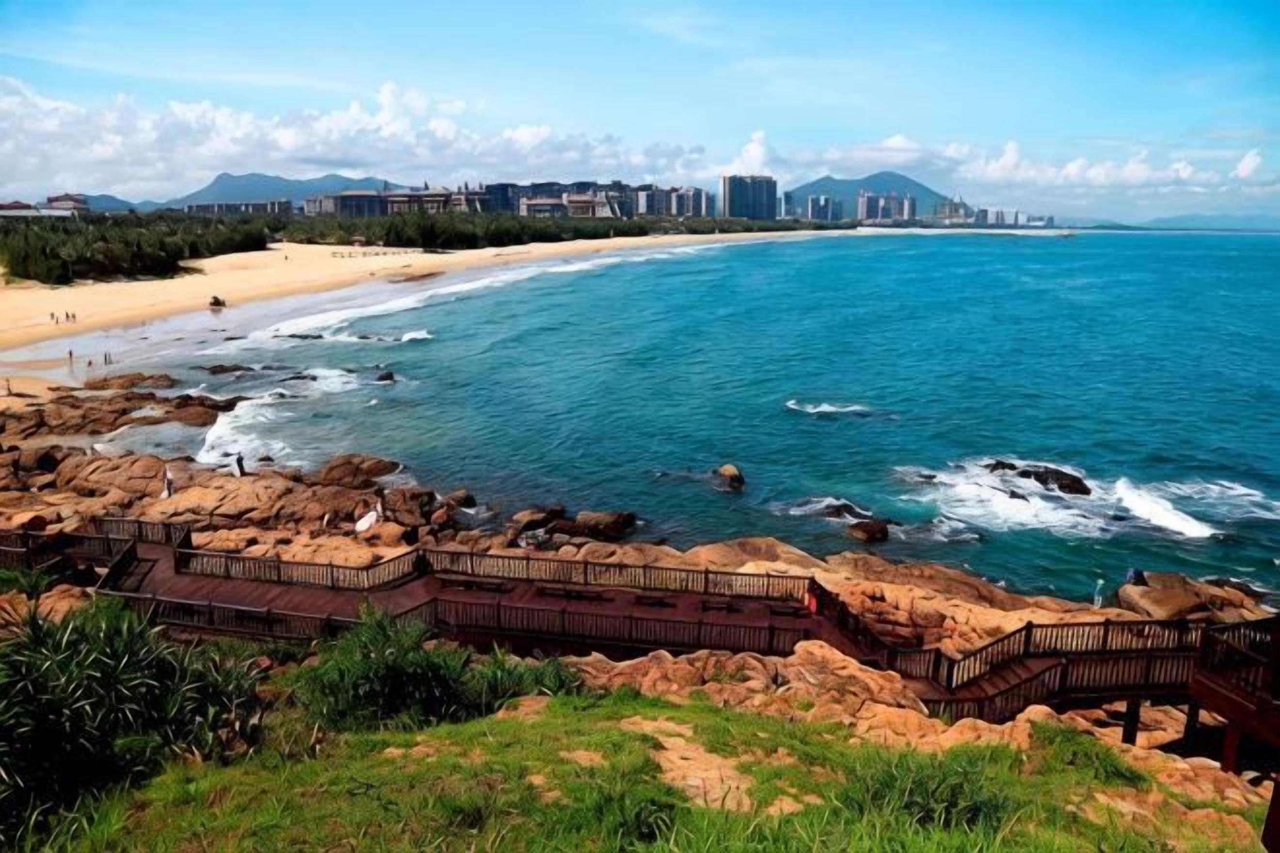 Paisagem costeira com uma linha de costa rochosa, uma praia e o horizonte de uma cidade ao longe.