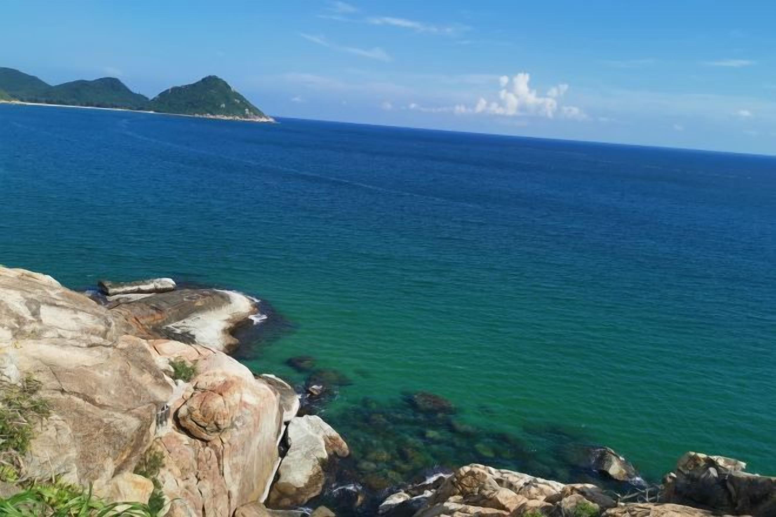 Paisagem costeira com águas azul-claras, formações rochosas e ilhas ao longe.