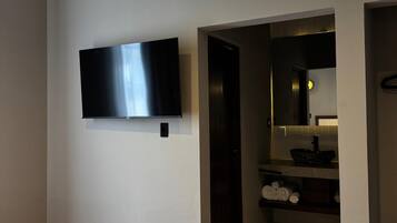 Quarto de hotel com televisão de tela plana na parede, piso de madeira e piso de azulejo no banheiro.