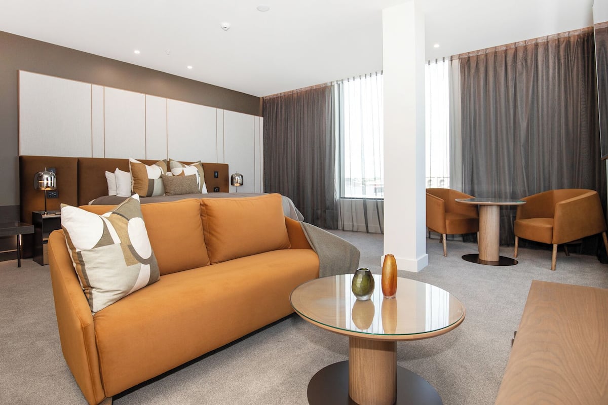 Quarto de hotel moderno com um sofá, uma mesa de vidro redonda e duas poltronas.