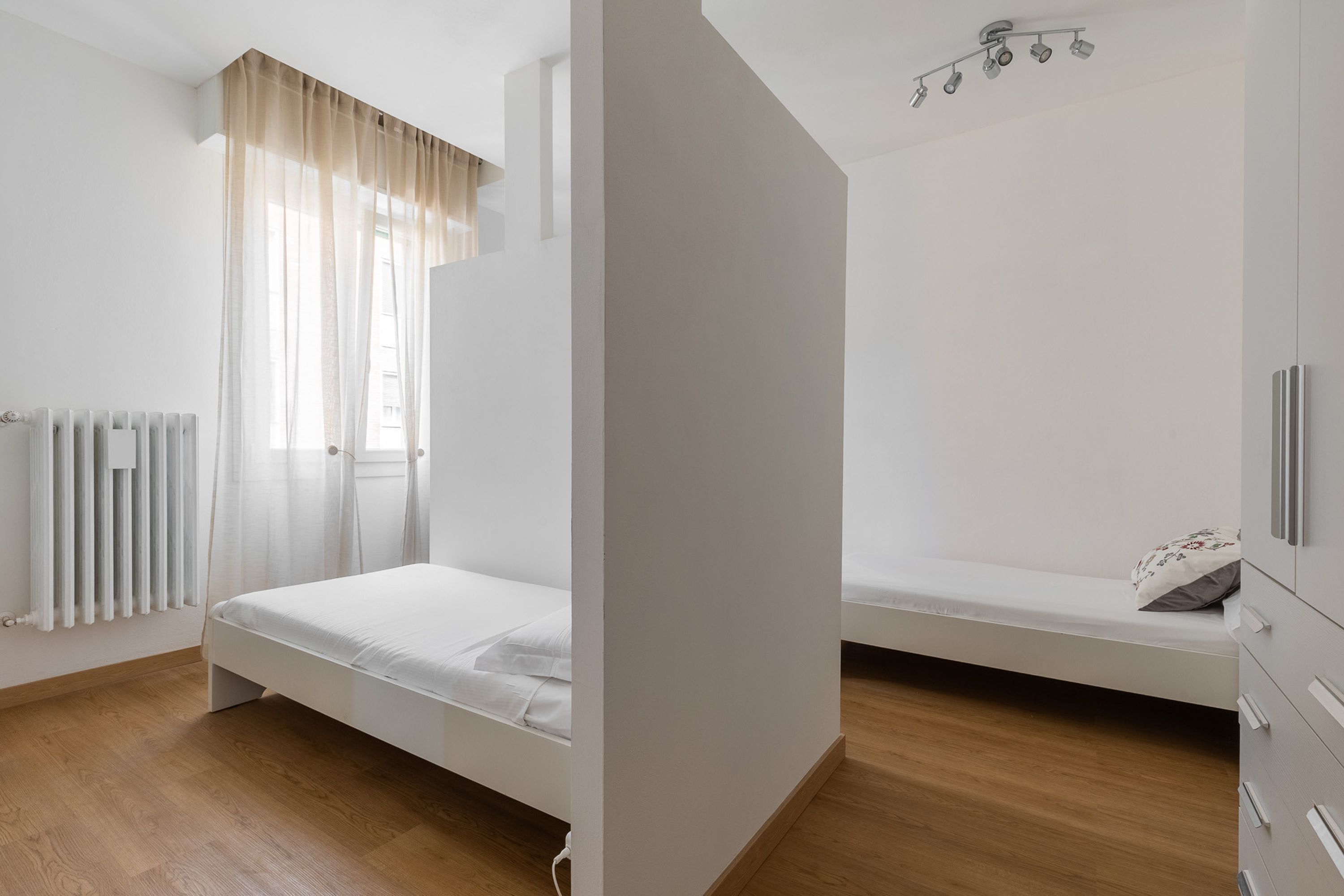 Quarto moderno e minimalista com uma cama de casal, um pequeno espaço de estar e um guarda-roupa.