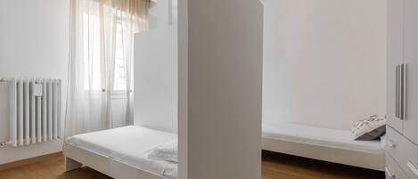Quarto moderno e minimalista com uma cama de casal, um pequeno espaço de estar e um guarda-roupa.
