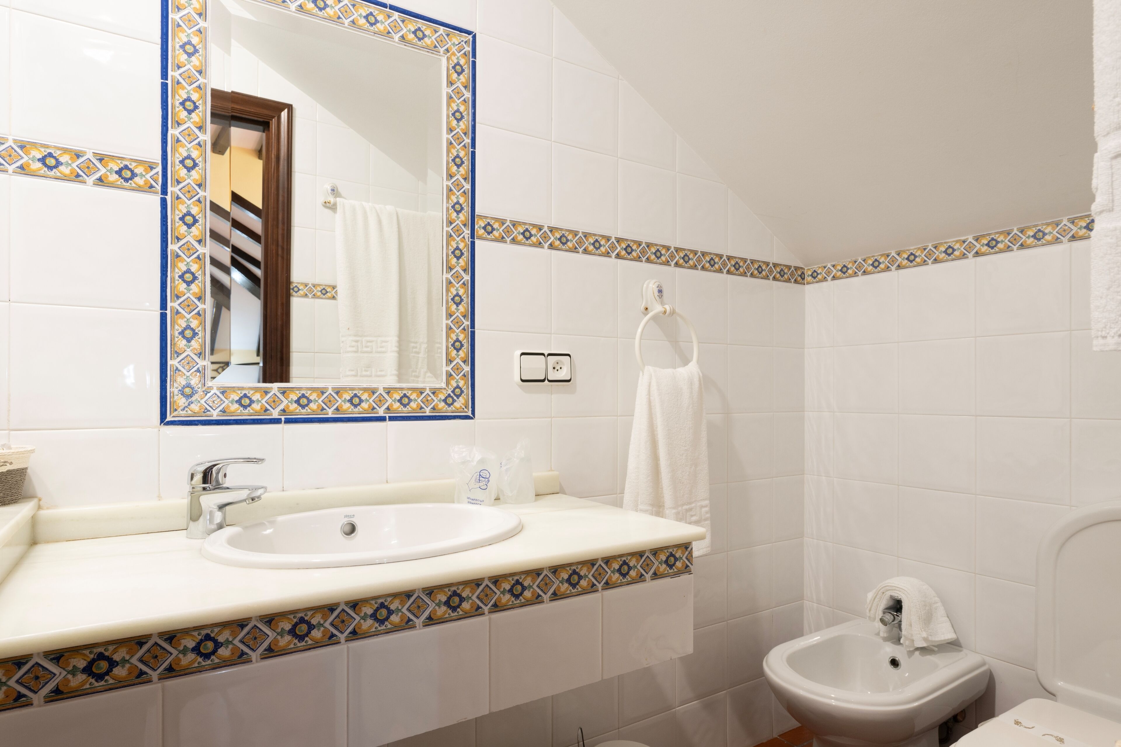 Um banheiro com pia branca, um espelho com moldura decorativa, um bidê e uma toalha pendurada na parede.