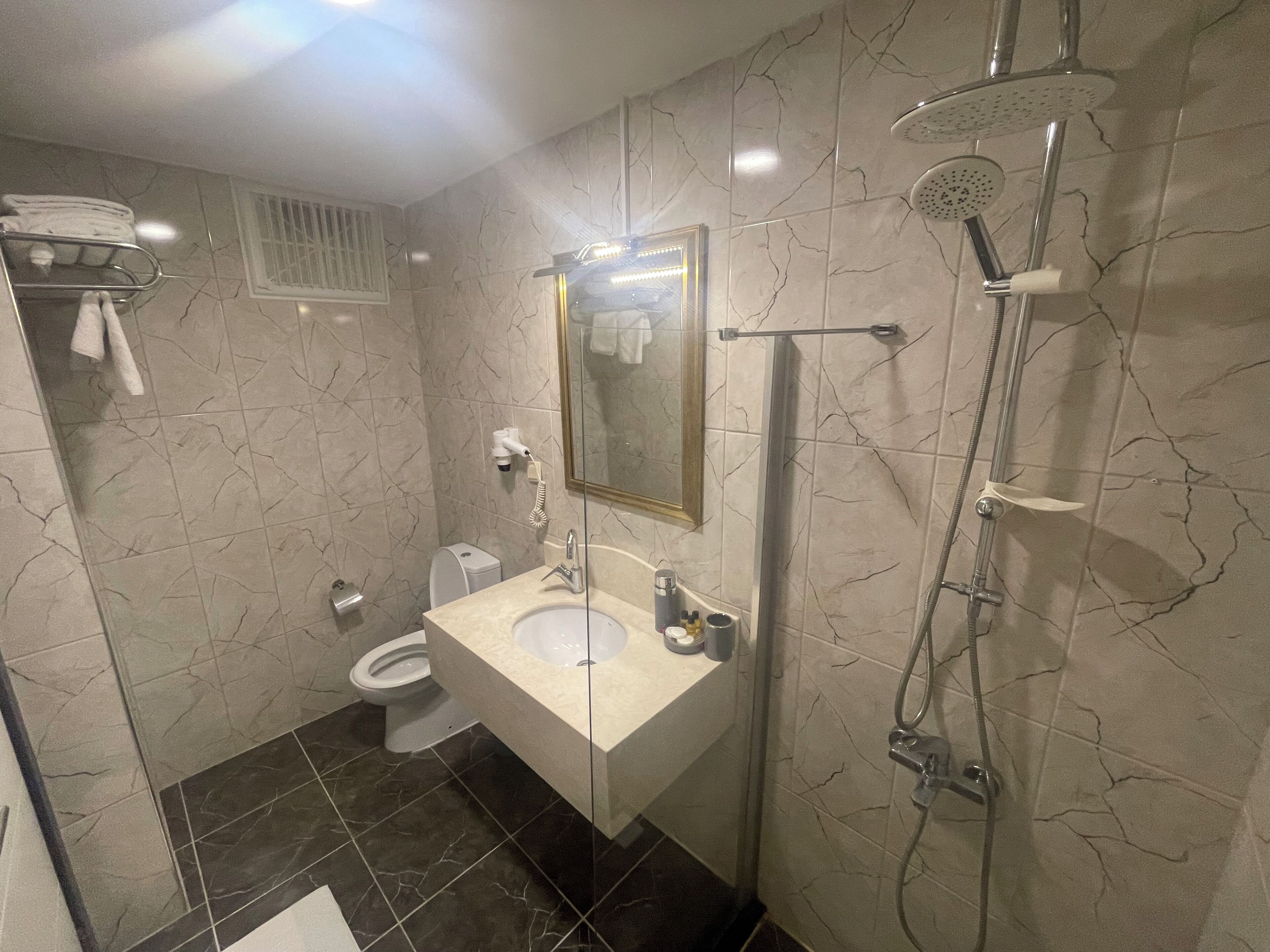 Um banheiro moderno com parede revestida em mármore, pia branca, box de vidro e vaso sanitário.