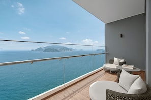 Varanda com vista para o mar, um sofá branco e uma pequena mesa com um livro.