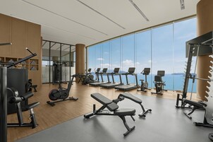 Academia moderna com equipamentos de cardio, máquinas de peso e bancos, com grandes janelas e uma vista panorâmica.