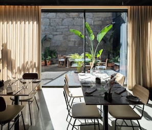Uma sala de jantar moderna com mesa e cadeiras de vidro, parede de pedra e plantas em vasos.