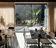 Uma sala de jantar moderna com mesa e cadeiras de vidro, parede de pedra e plantas em vasos.