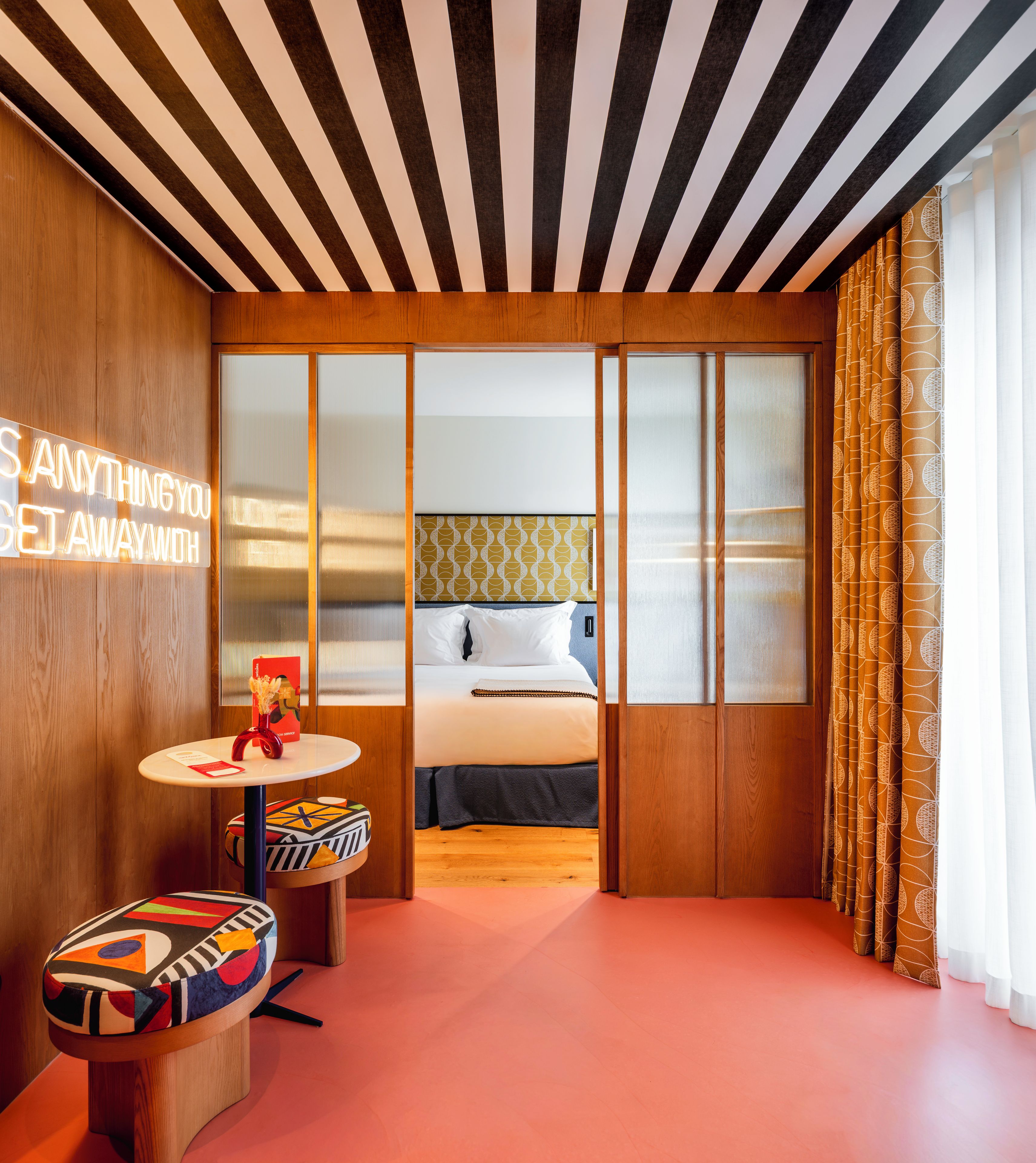 Quarto de hotel com uma cama, uma mesinha com um vaso e um quadro na parede.