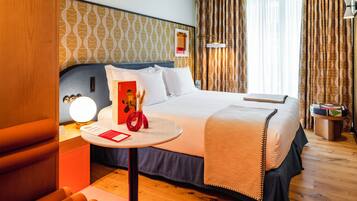 Quarto de hotel com cama, mesa de cabeceira, luminária e cortinas.