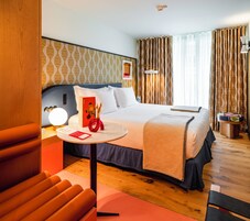 Quarto de hotel com cama, mesa de cabeceira, luminária e cortinas.