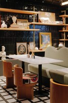 Um interior moderno com um sofá, uma mesa e uma cadeira. Estantes com diversos objetos e um quadro na parede.