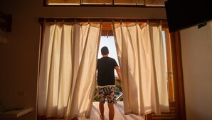 Uma pessoa caminhando por uma porta com cortinas, que dá para uma área externa com piso de azulejos.