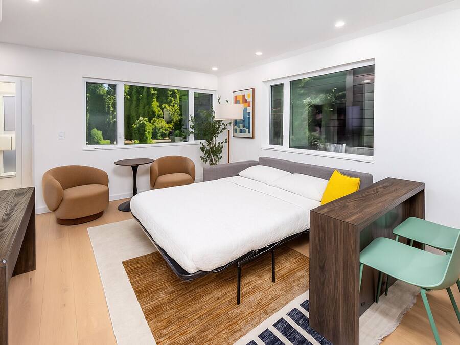 Quarto moderno com cama, duas poltronas, uma mesinha e uma escrivaninha.