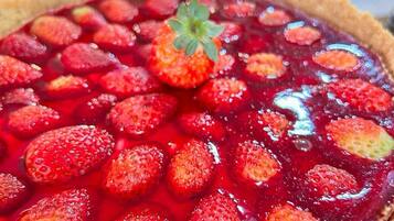 Uma tarte de morango com borda crocante e recheio vermelho brilhante, coberta com morangos inteiros e um único morango no centro.