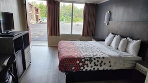 Quarto de hotel com cama, escrivaninha, cadeira e televisão.