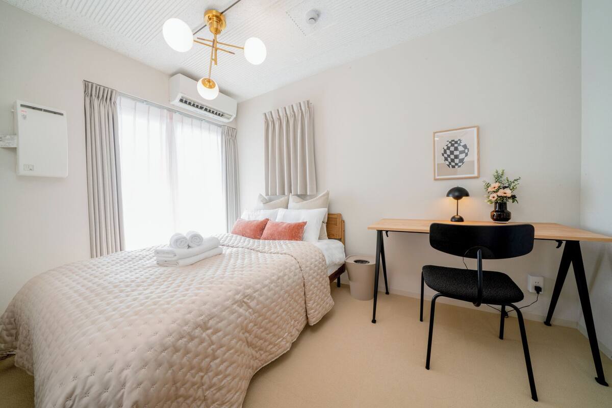 Quarto de hotel com cama, escrivaninha, cadeira e ventoinha no teto.
