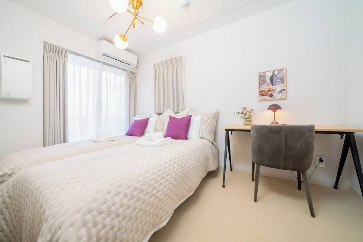 Quarto de hotel com cama, escrivaninha, cadeira e luminária no teto.