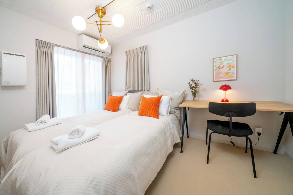 Quarto de hotel com cama, escrivaninha, cadeira, ar condicionado e janela com cortinas.