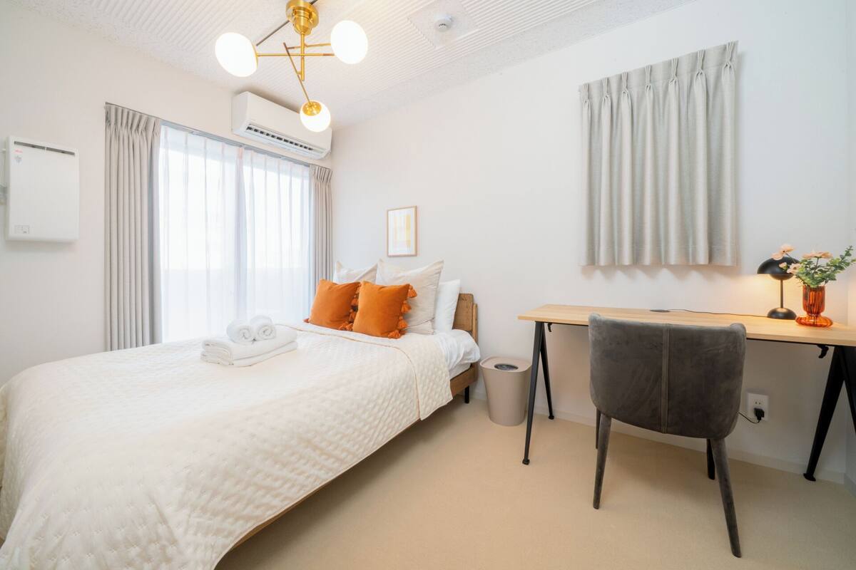 Quarto de hotel com cama, secretária, cadeira e janela com cortinas.