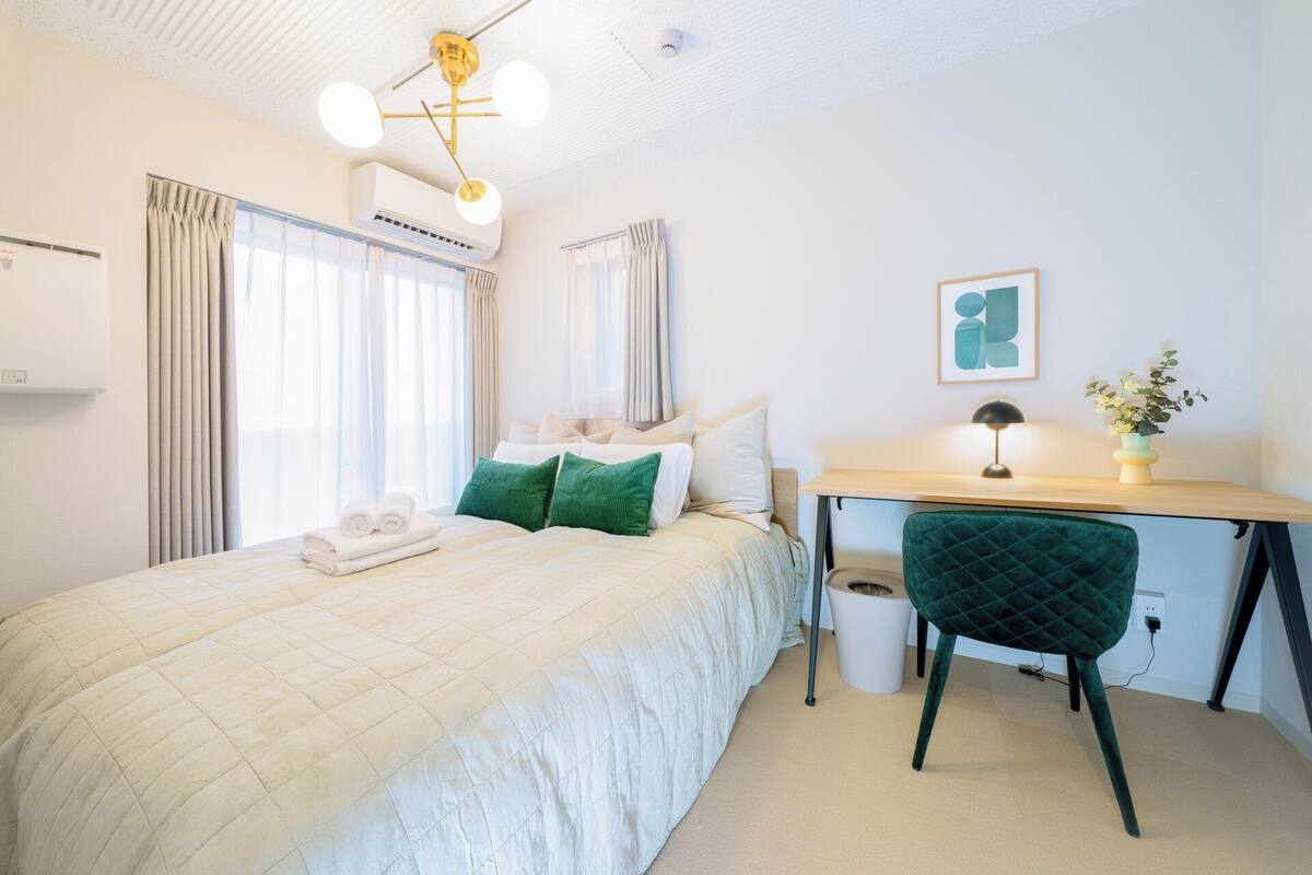 Quarto de hotel com cama, escrivaninha, cadeira, abajur e quadro na parede.