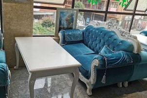 Quarto com mesa branca, sofá azul e uma grande janela com vista para o exterior.