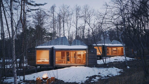 Uma cabana com fachada de vidro, lareira e paisagem coberta de neve.