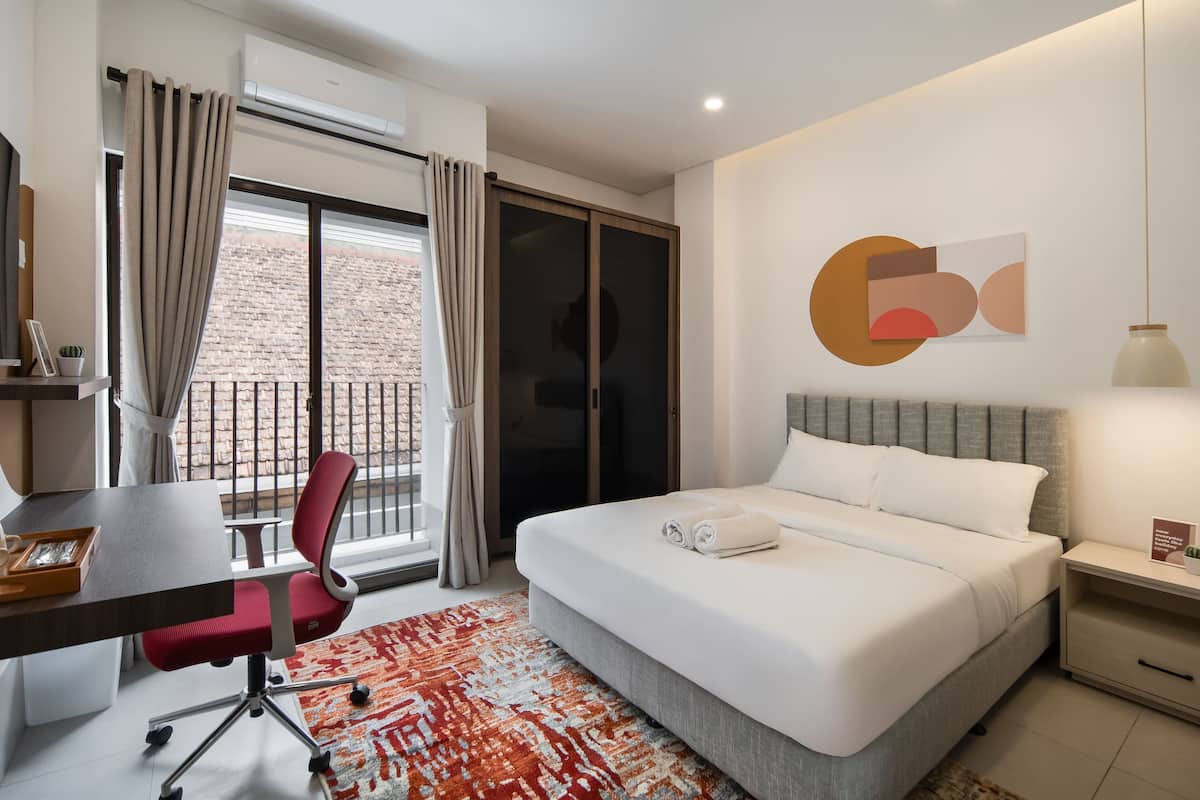 Quarto de hotel com cama, escrivaninha, cadeira e vista para o exterior.
