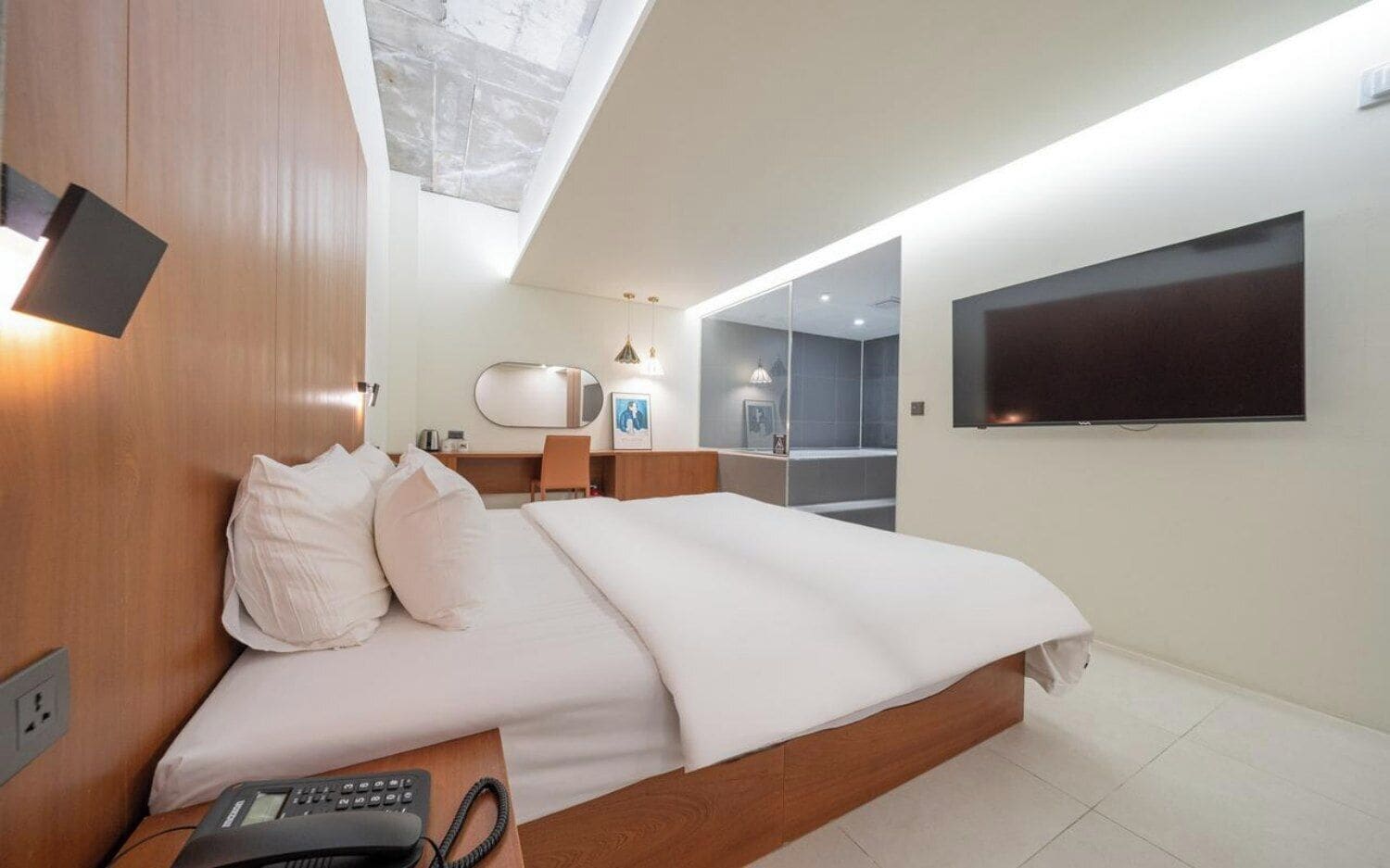 Quarto de hotel moderno com uma cama grande, mesa de cabeceira e televisão montada na parede.