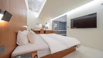 Quarto de hotel moderno com uma cama grande, mesa de cabeceira e televisão montada na parede.