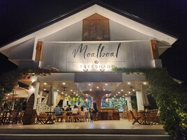 Um restaurante chamado "Moalboat", com uma placa, área de estar ao ar livre e um mural com tema tropical ao fundo.