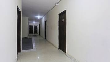 Um corredor comprido e estreito, com paredes brancas e chão em azulejos. Há portas em ambos os lados, uma delas com o número 302.