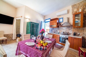 Uma área de refeições com mesa posta para dois, uma cozinha com fogão e forno, e uma parede de pedra.